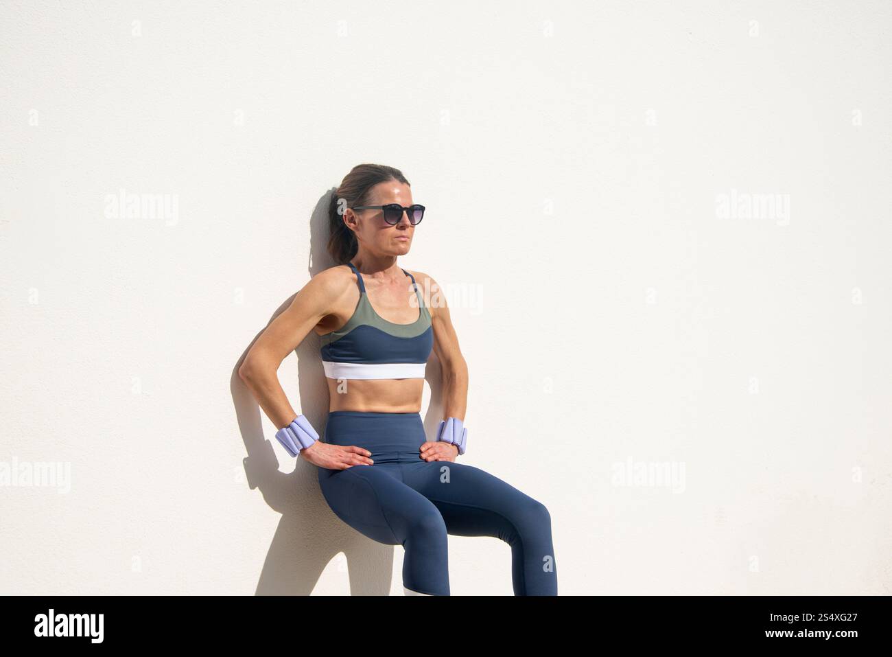 sporty woman wearing adjustable wrist weights doing a wall squat ...