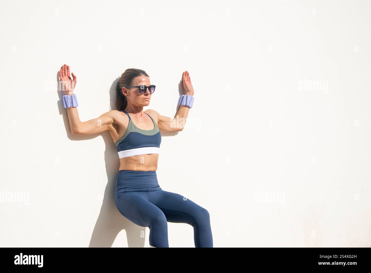 sporty woman wearing adjustable wrist weights doing a wall squat ...