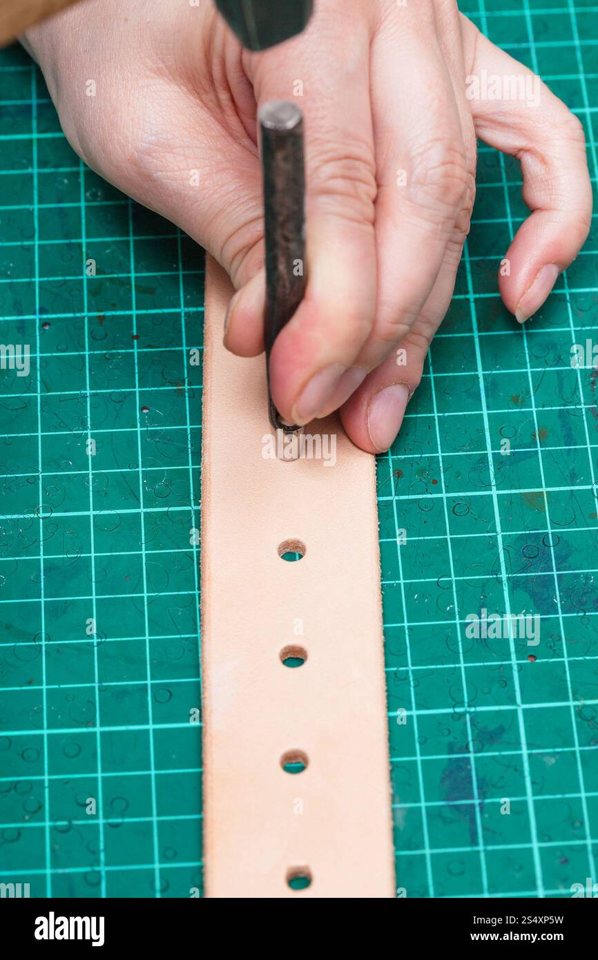 punching holes in new leather belt with hole punch on self-healing mat ...
