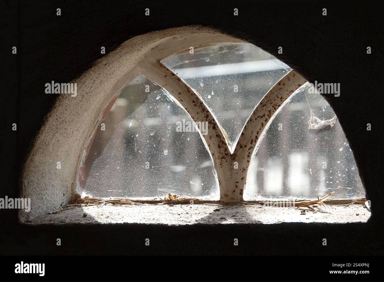 An antique half-round window with dirt and cobwebs. The light comes ...