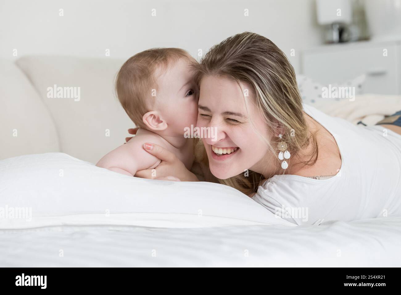Portrait of happy laughing mother playing with her baby boy on bed ...