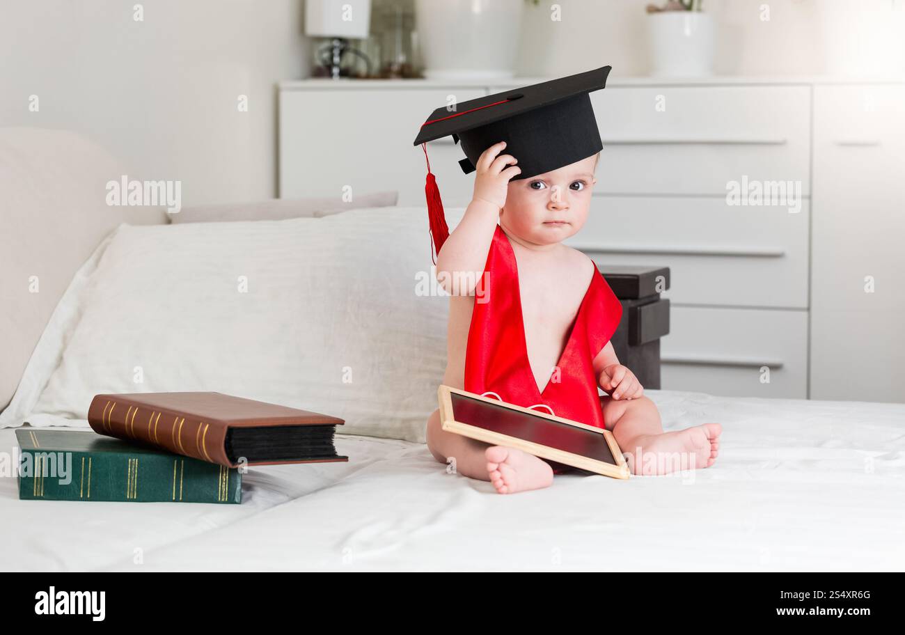 Funny portrait of 10 months old baby boy with books wearing graduation ...