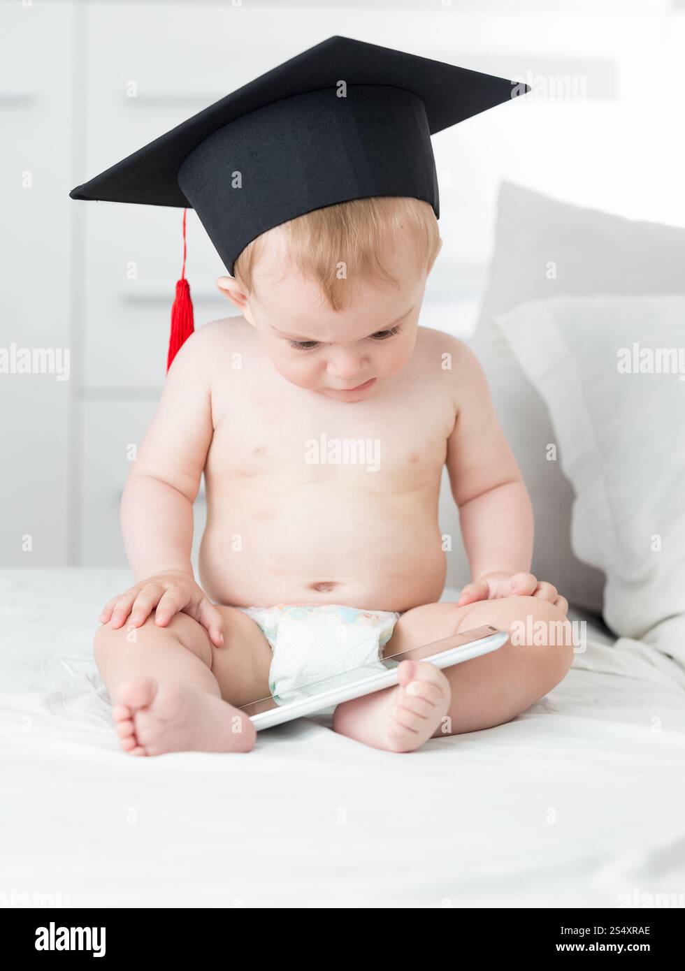 10 months old baby boy in diapers wearing graduation cap and using ...