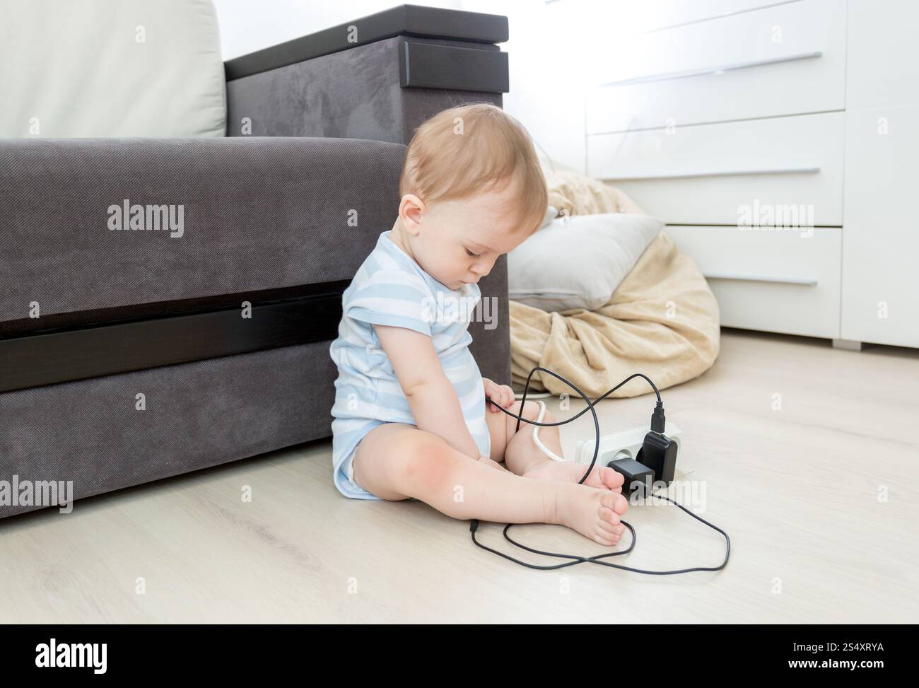 Little baby sitting alone in living room and playing with electrical ...