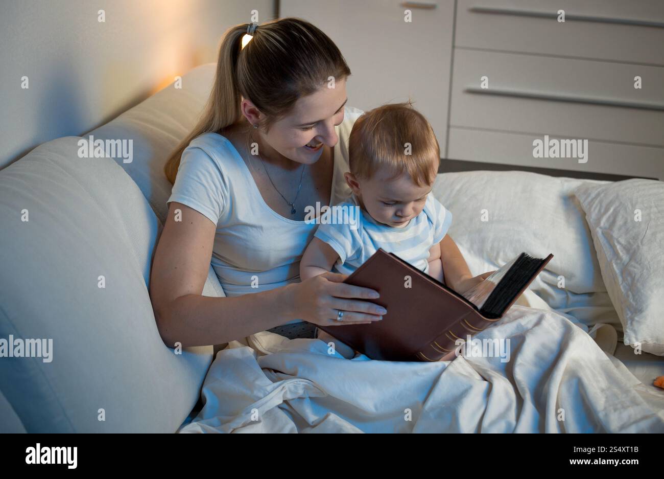Young mother storytelling to her adorable baby boy at bed before going ...