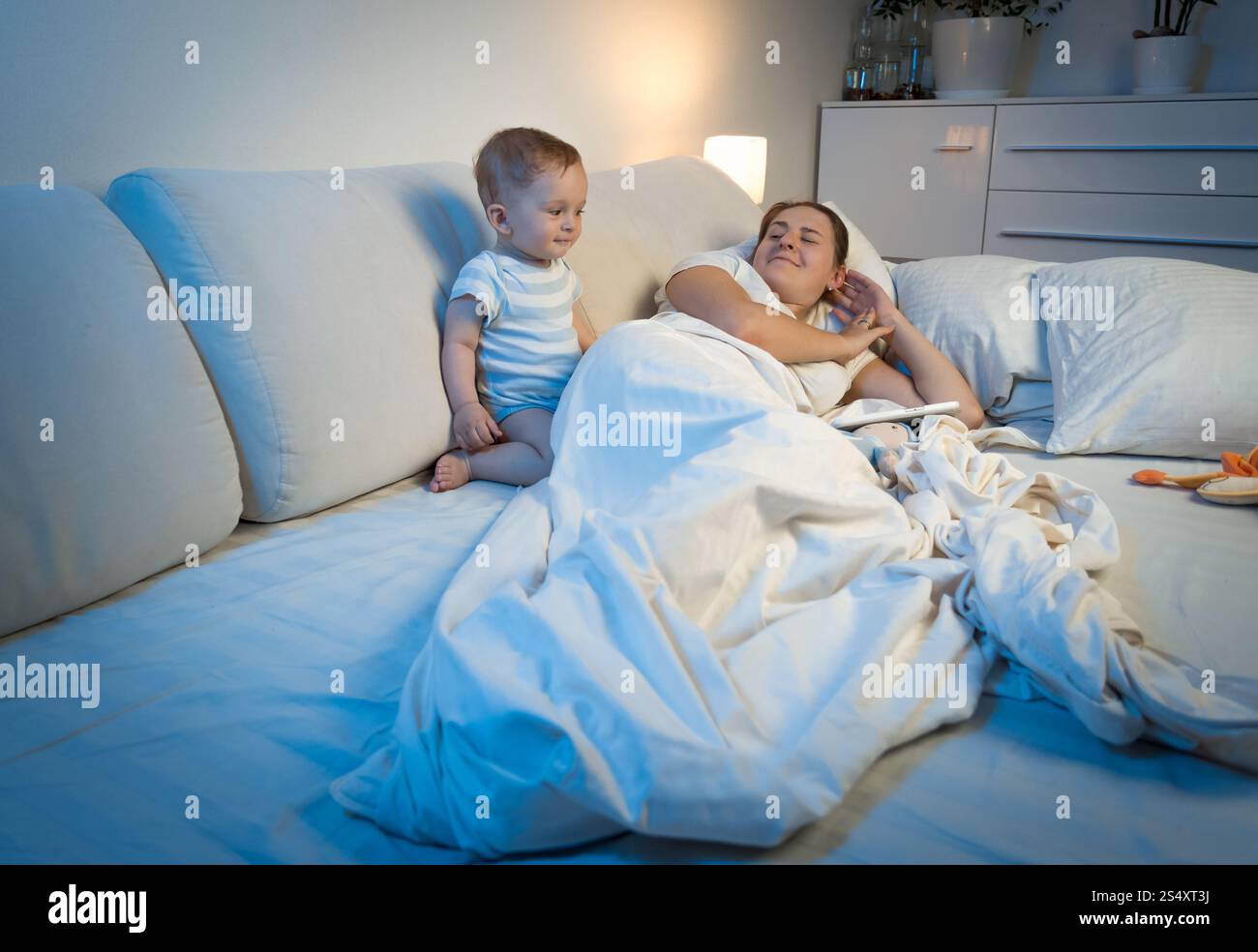 Sleepless baby boy waking up mother sleeping in bed Stock Photo - Alamy