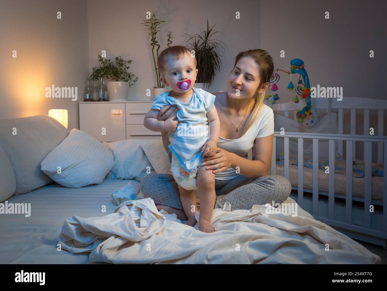 Young mother changing messy diapers to her baby boy on bed at night ...