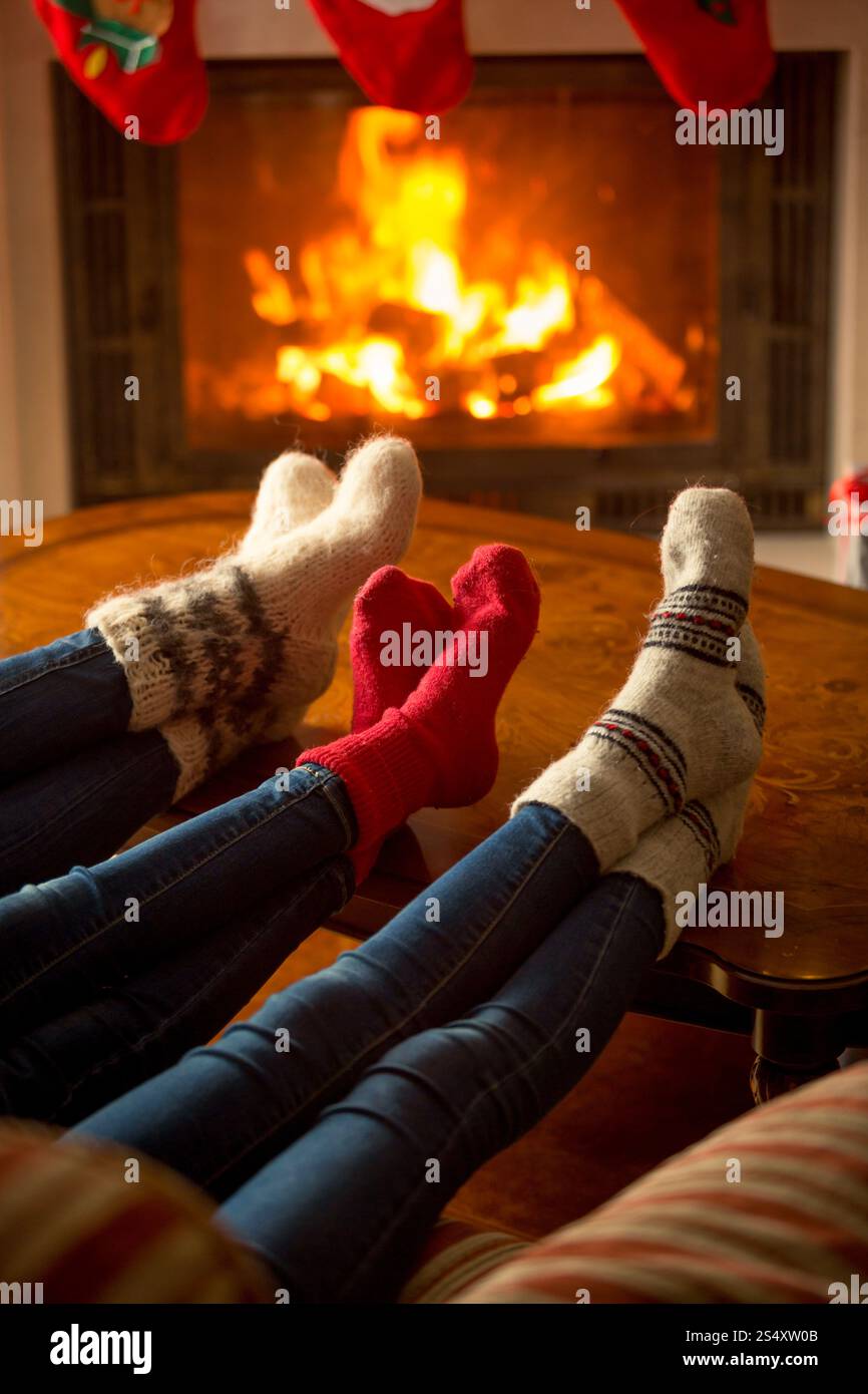 Three pair of feet in woolen socks warming at burning fireplace at ...