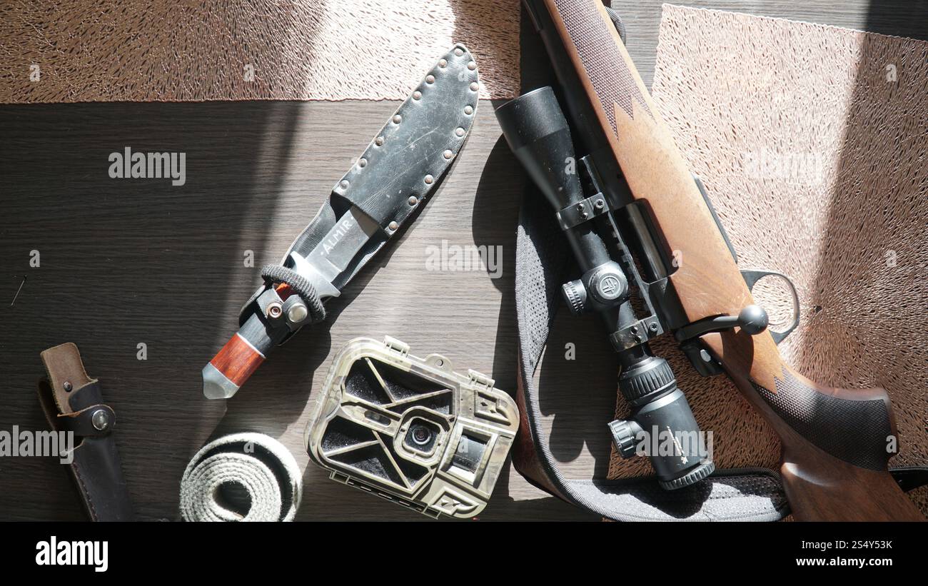 Hunting rifle with hunting equipment on a wooden table, sunlight is ...