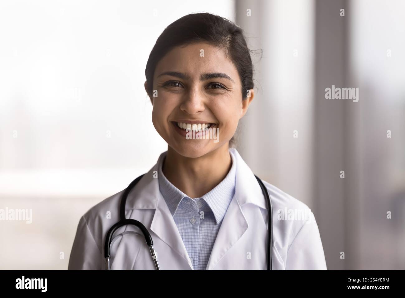 Happy Indian female cardiologist in white coat posing at workplace ...