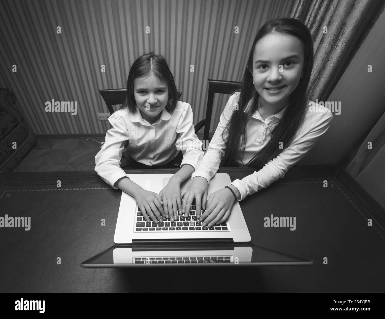Black and white portrait of two teen girls using laptop at cabinet ...