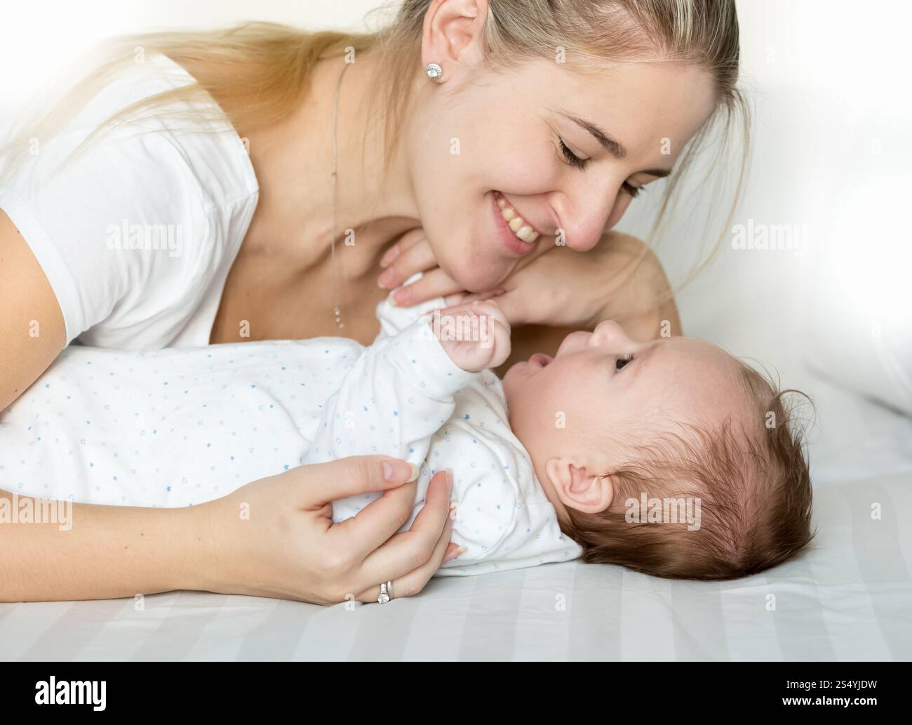 Portrait of beautiful young mother cuddling her baby boy on bed Stock ...