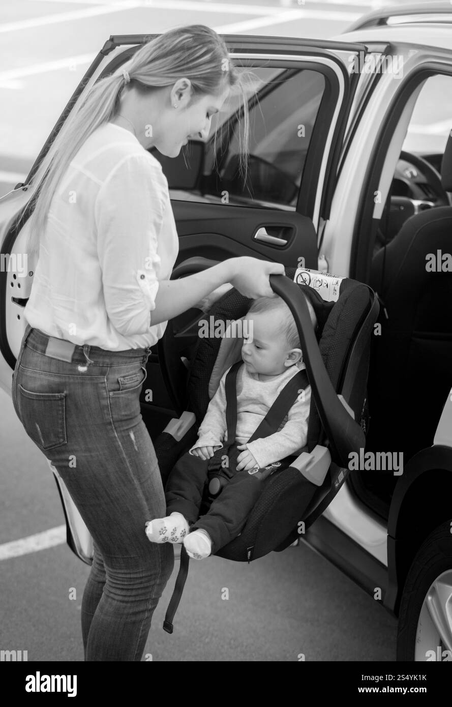 Black and white image of young mother putting car seat with her baby ...