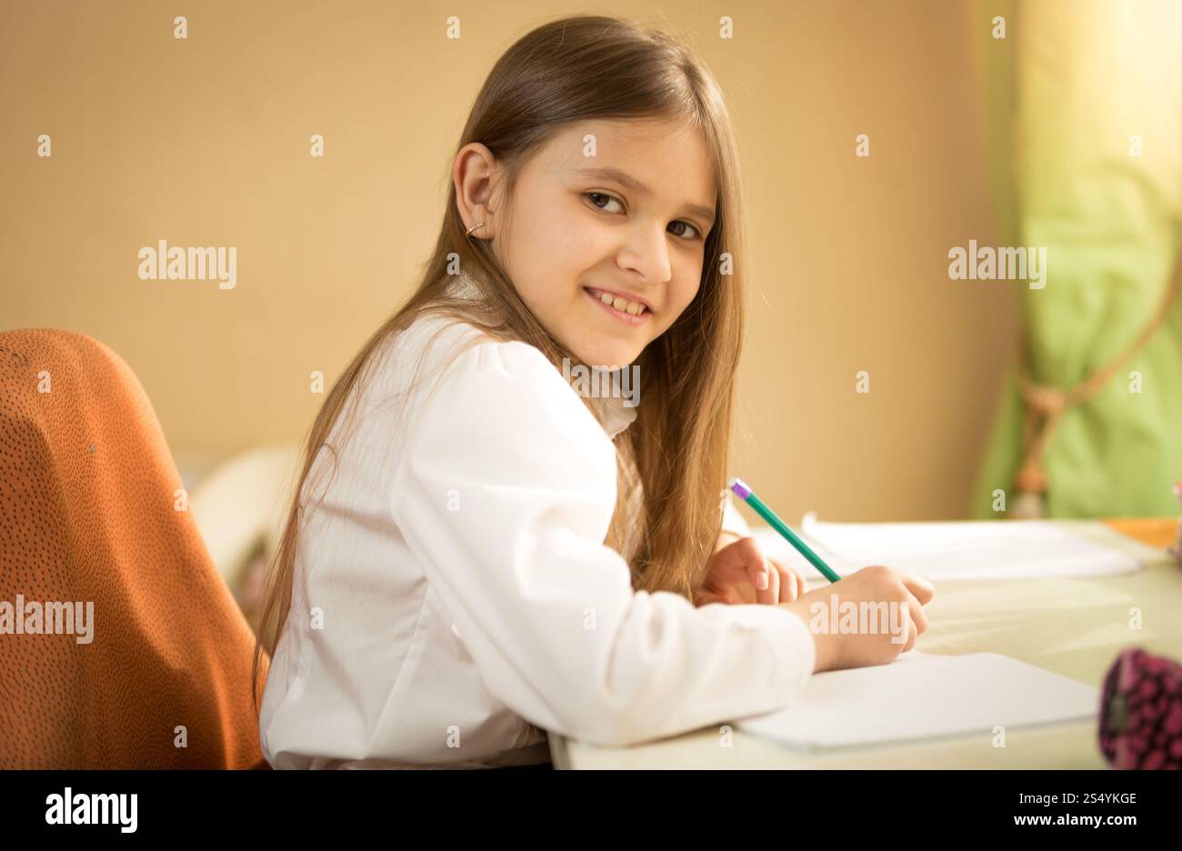 Portrait of smiling girl in white shirt sitting behind desk and doing ...
