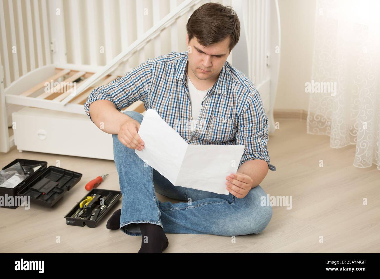 Puzzled man reading assembly instructions to babys cot Stock Photo - Alamy