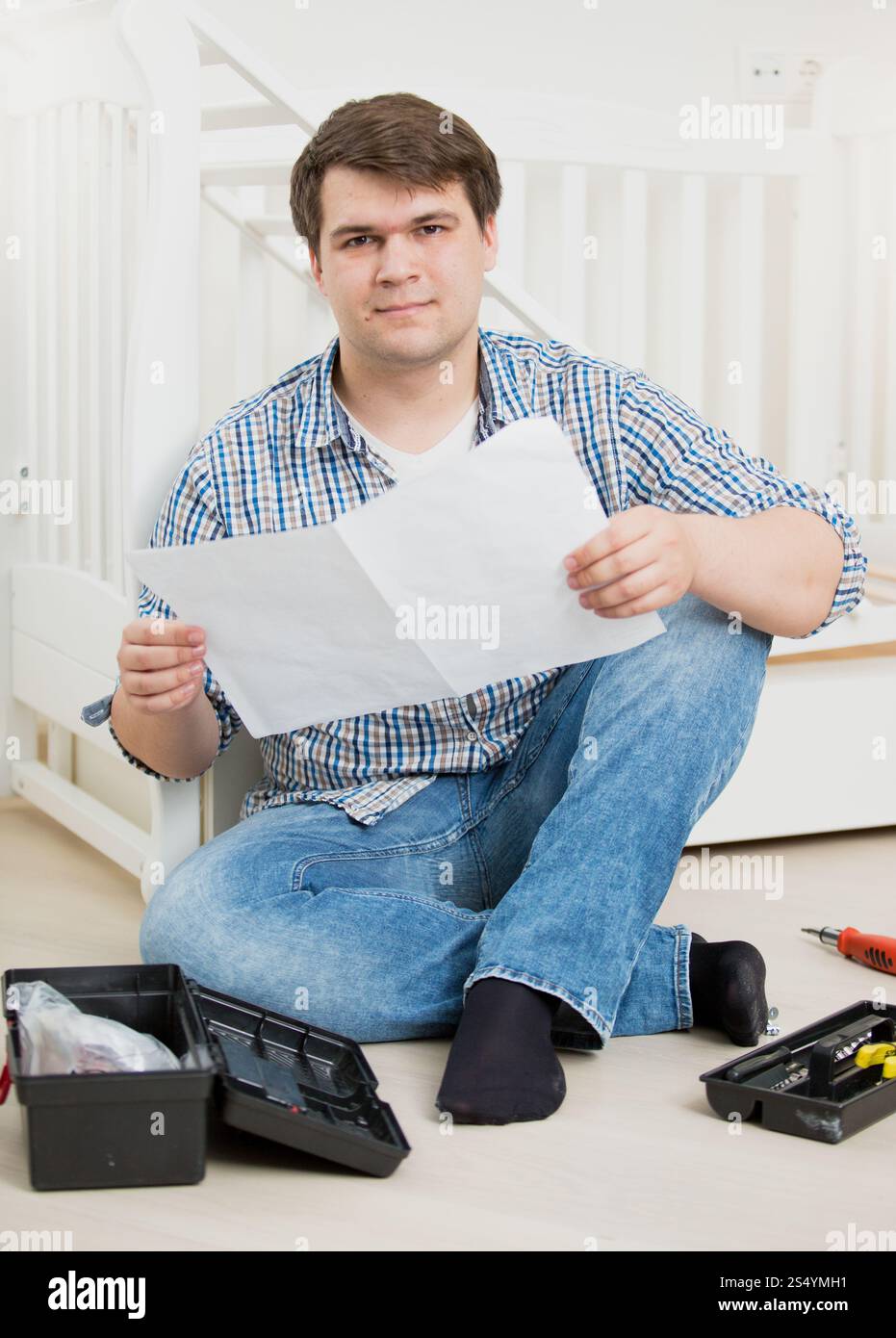 Puzzled man reading assembly instructions to babys cot Stock Photo - Alamy