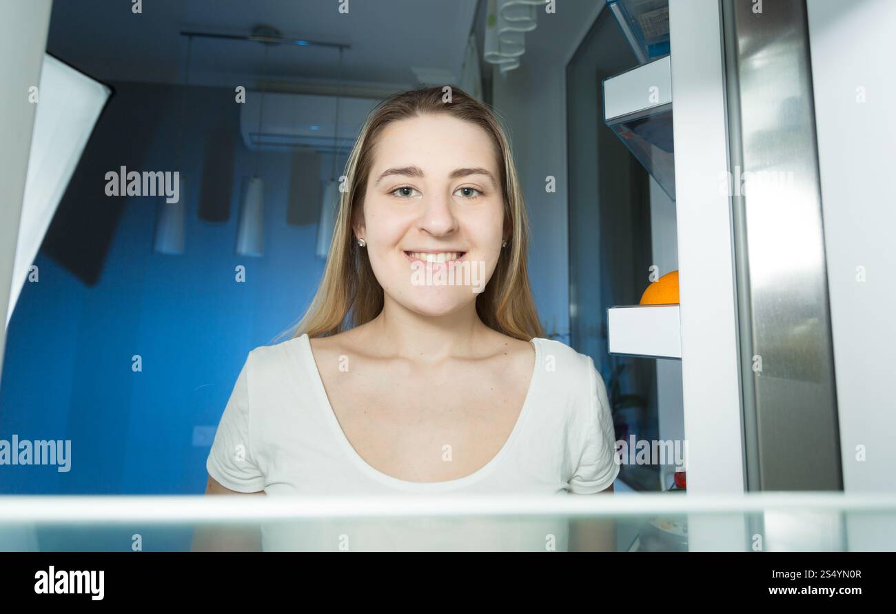 Woman in pajamas looking inside the refrigerator at home at late night ...