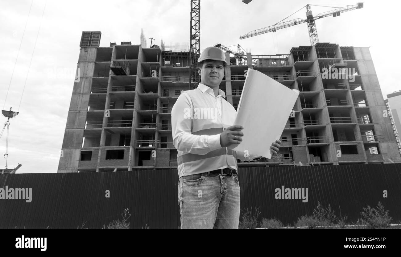 Black and white portrait of young engineer in hardhat with blueprints ...
