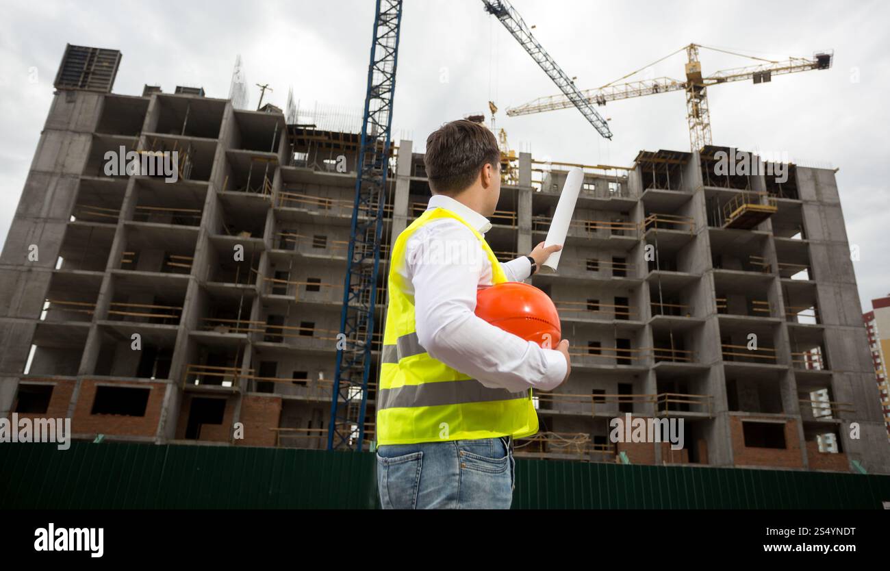 Young engineer pointing at building with rolled blueprints Stock Photo ...