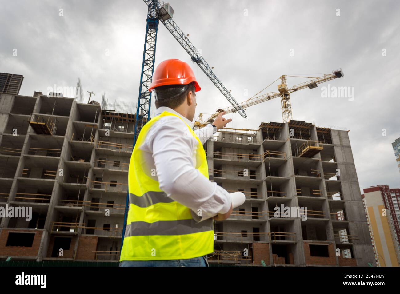 Young architect holding blueprints and pointing at building under ...