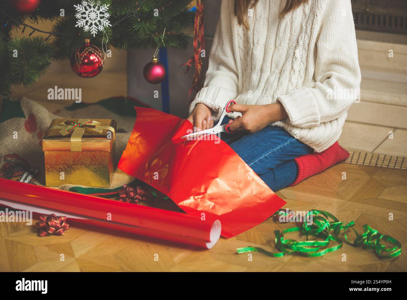 Cute girl cutting wrapping paper under Christmas tree at living room ...
