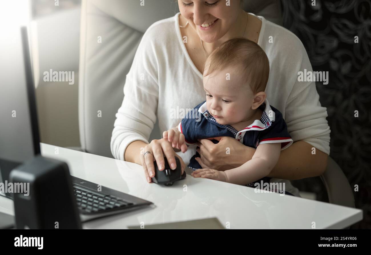 Cute baby boy sitting on mothers lap and playing with computer mouse ...