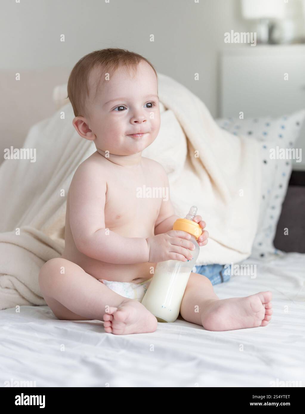Baby boy in diapers sitting on sofa and holding bottle with milk Stock ...