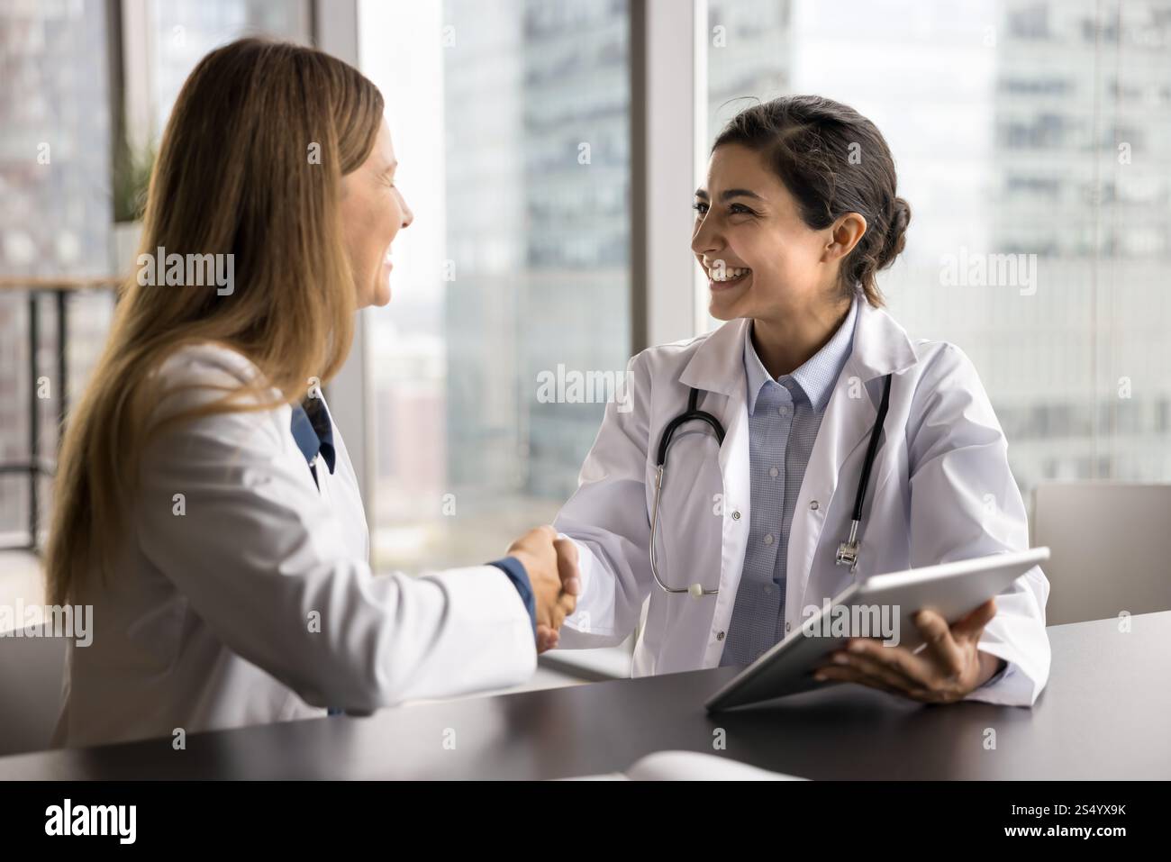 Two women doctors shaking hands while sitting across table Stock Photo ...