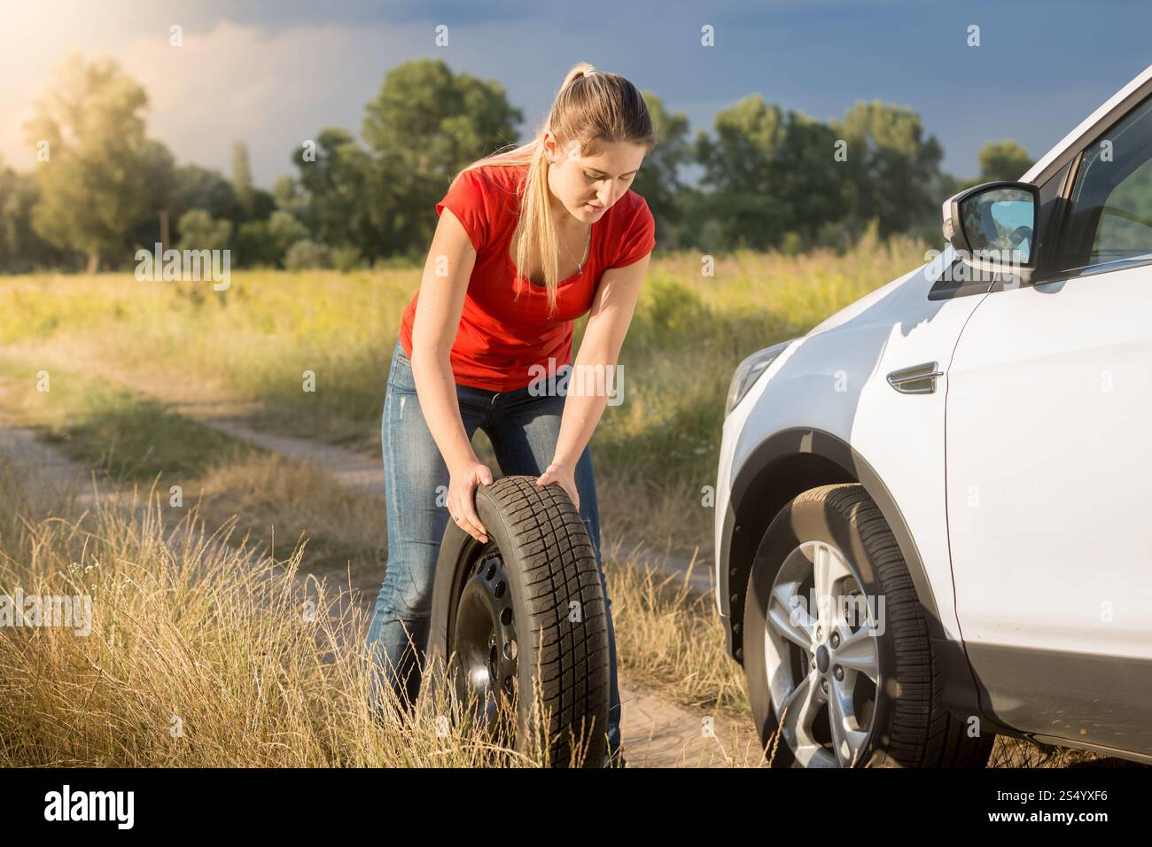 Young woman rolling spare tire to change the flat one Stock Photo - Alamy