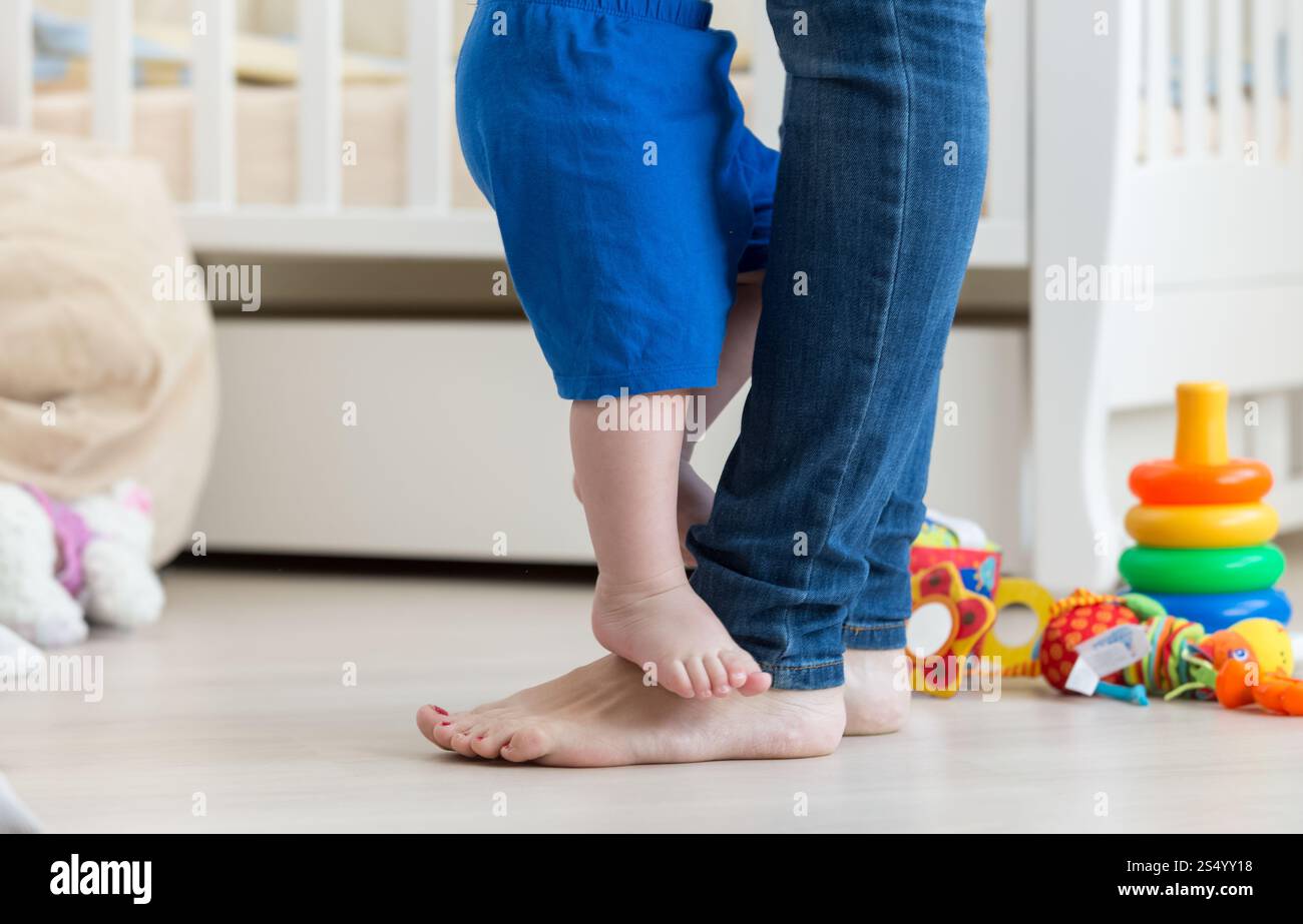 Closeup photo of babys feet standing in front of mothers feet on floor ...