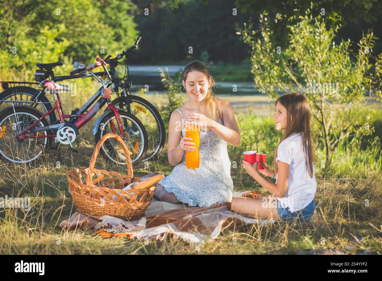 Mother having picnic by the river with daughter. Mother pouring orange ...