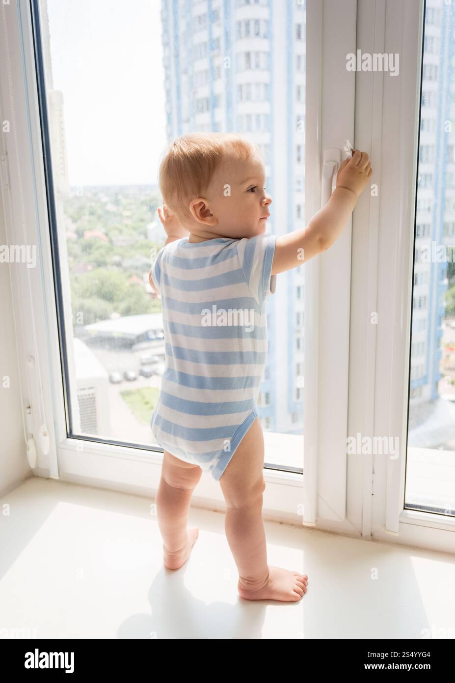 Little baby boy standing on window sill and pulling window handle Stock ...