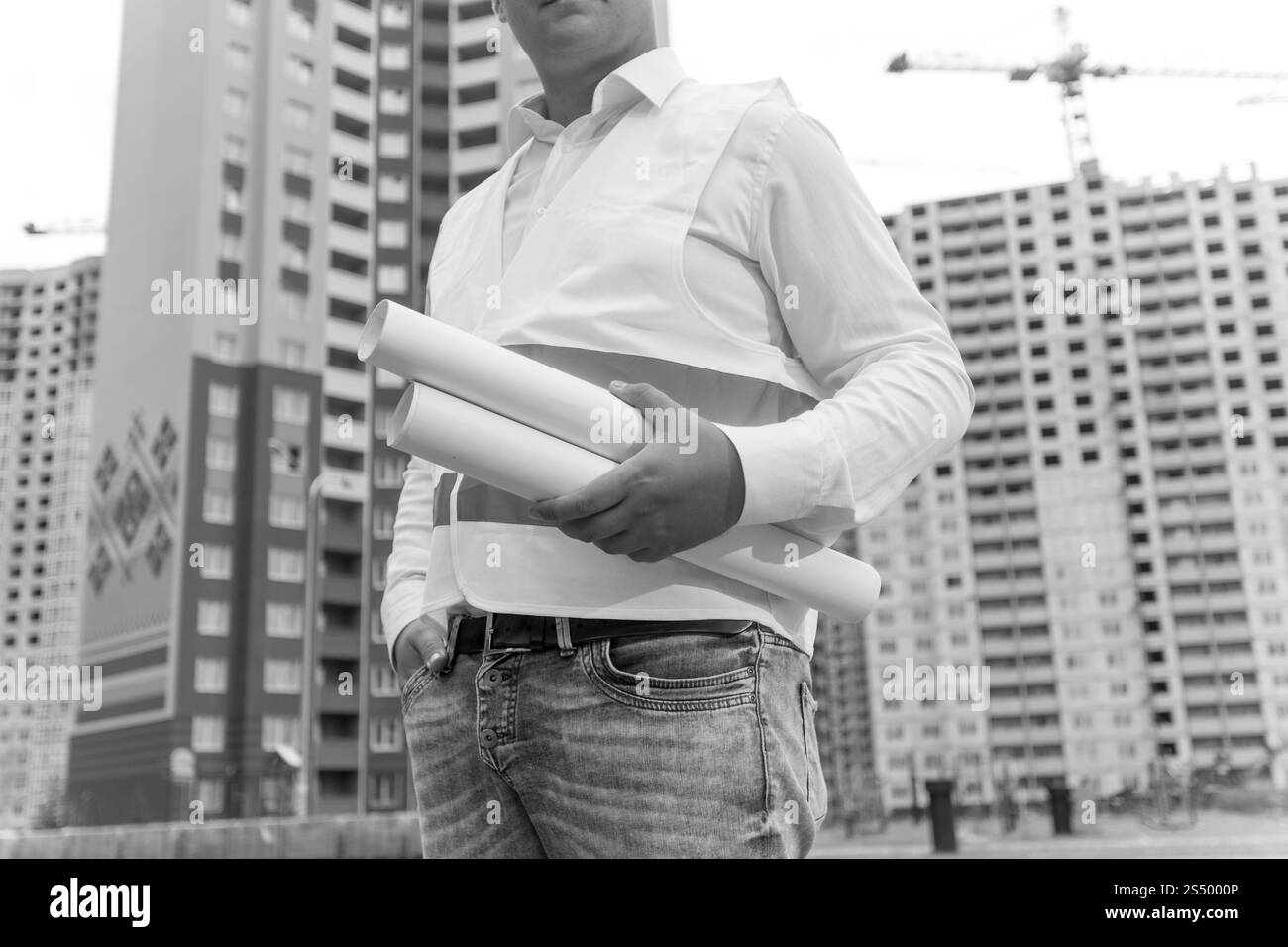 Closeup Black And White Photo Of Engineer Holding Rolled Blueprints In Background Of Building