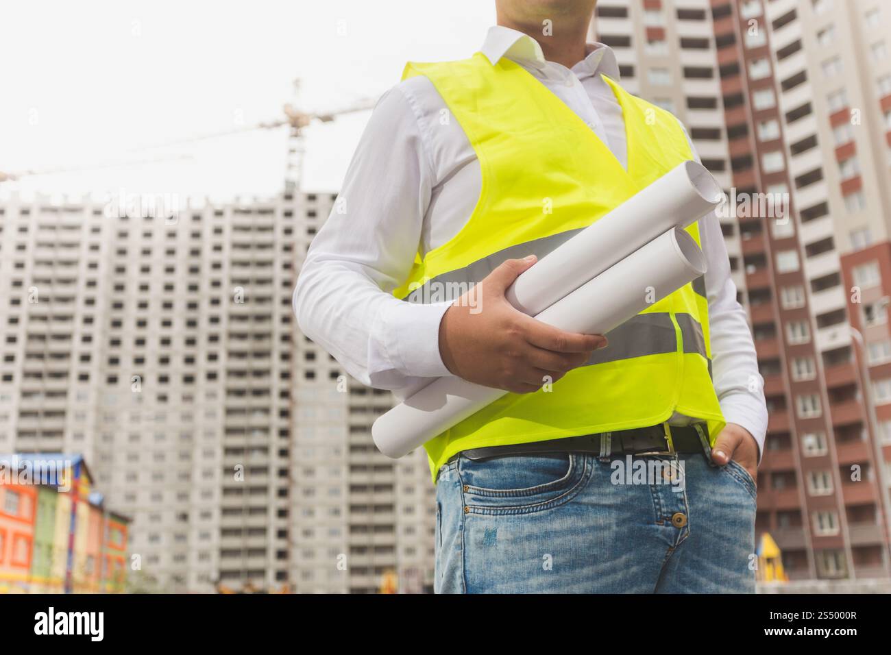 Architect in safety vest posing with blueprints at new buildings Stock ...