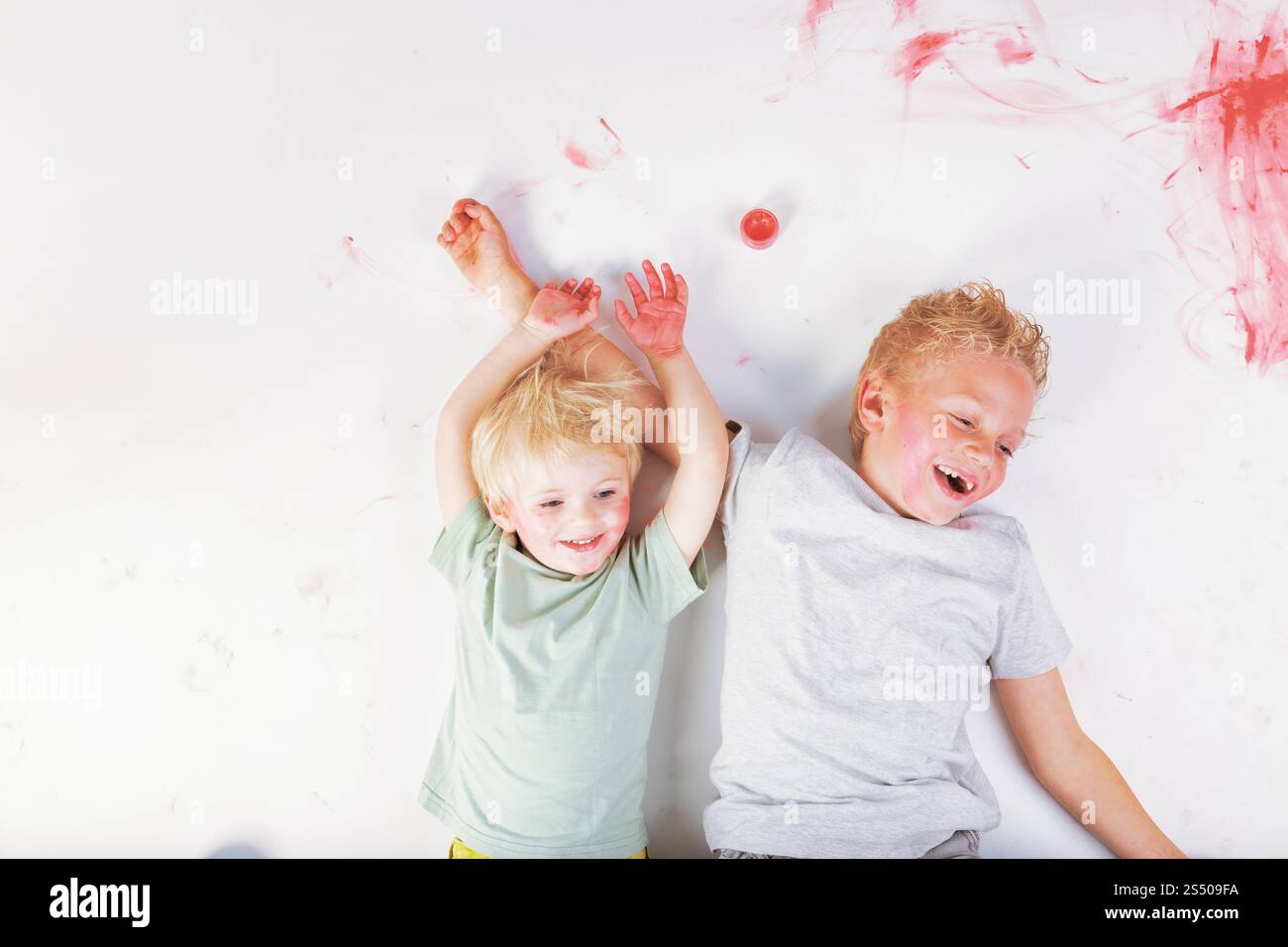 Two blond preschool brothers lying on a white surface, covered in pink ...