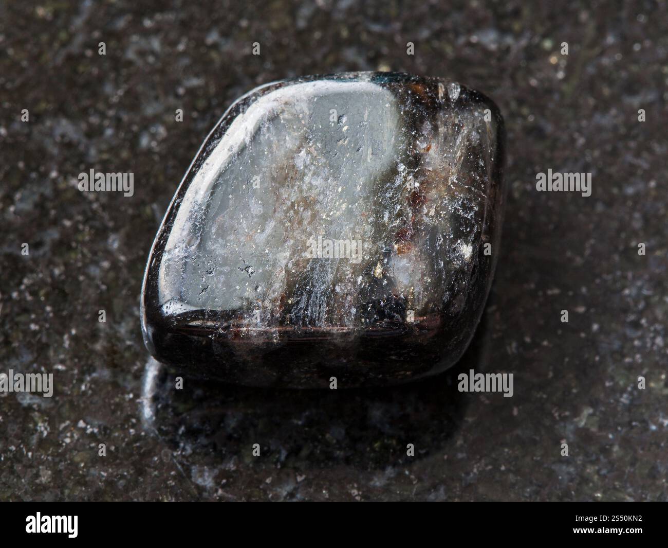 macro shooting of natural mineral rock specimen - tumbled anthophyllite gemstone on dark granite ...