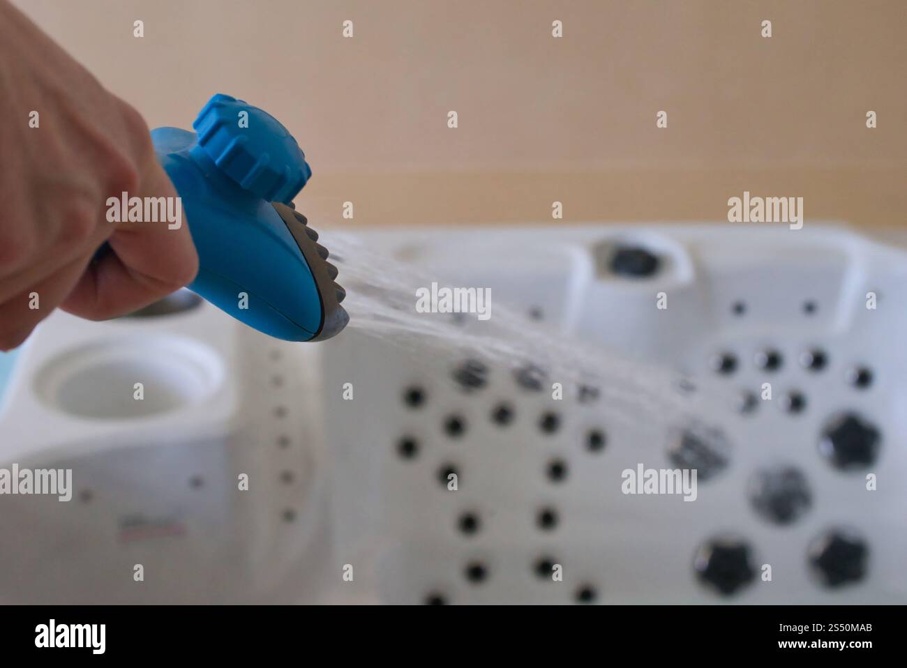 Hand holding a blue pool cleaning nozzle, spraying water onto whirlpool ...
