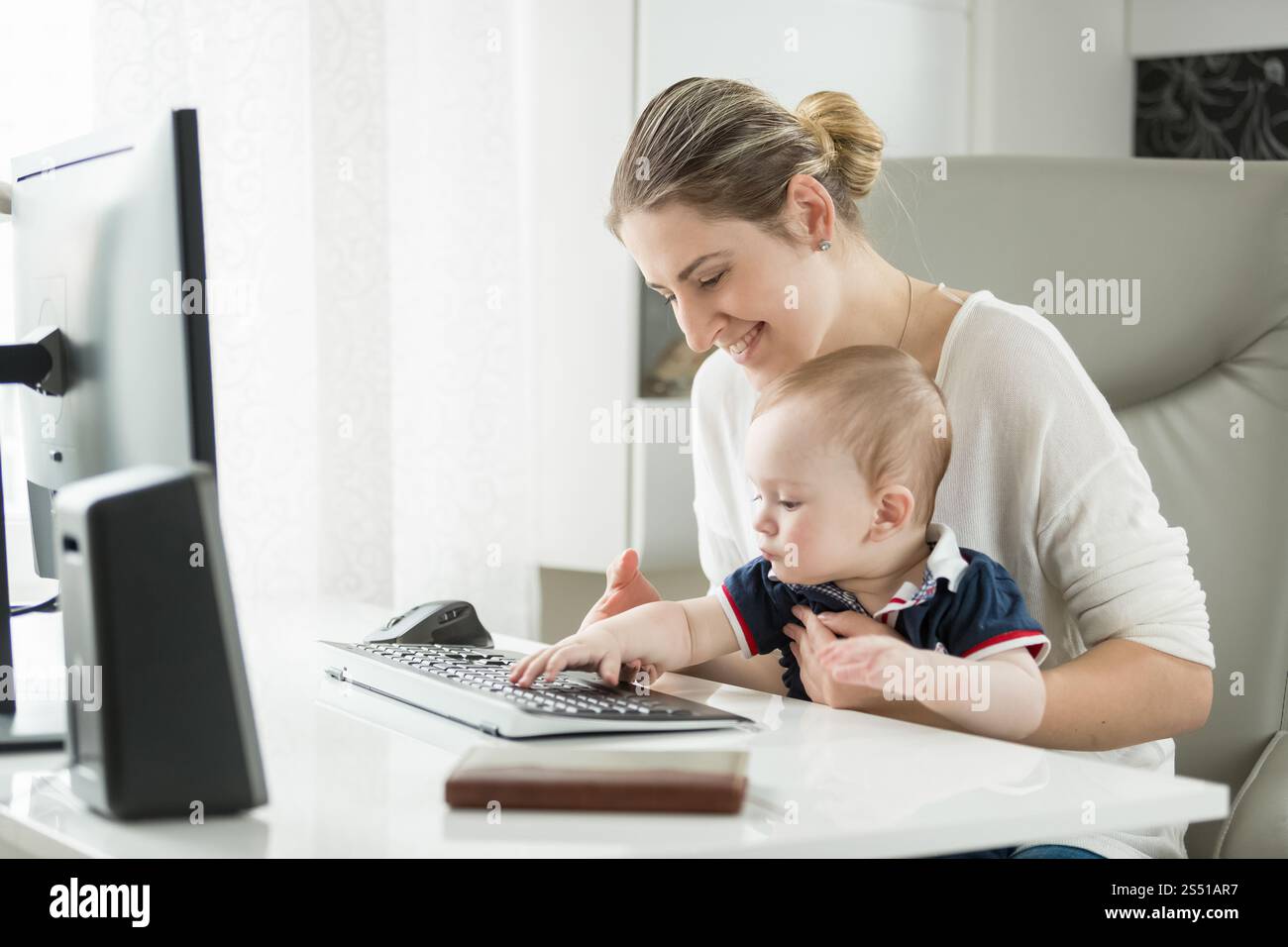 Portrait of young mother teaching her baby son using computer and ...