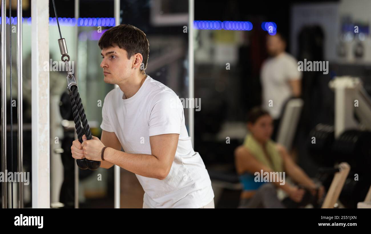 Guy in gym performs exercises for arm muscles using cable crossover ...