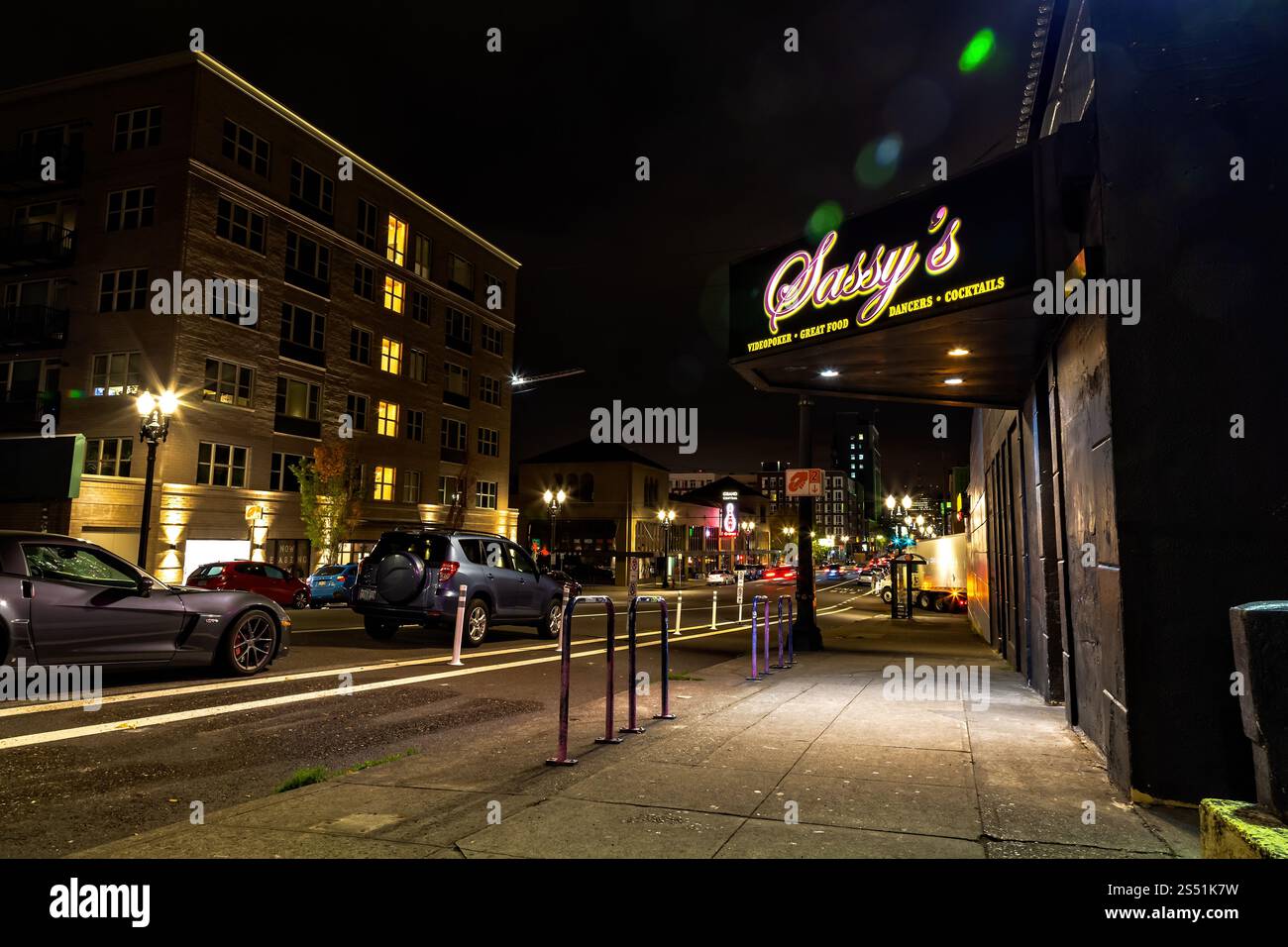 City Street at Night with Illuminated Shop Signs and Passing Cars ...