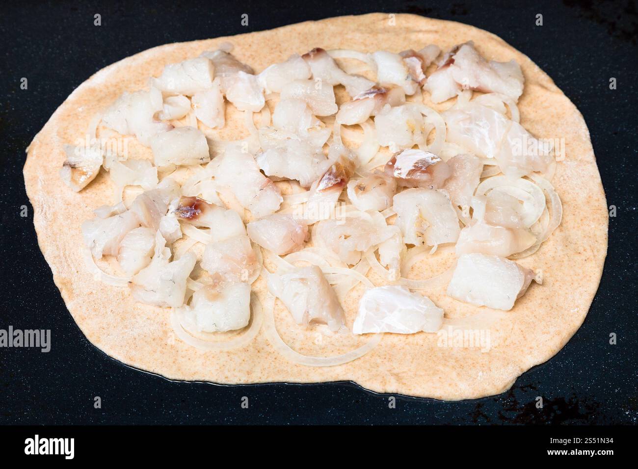 cooking of pie - sheet of dough with stuffing from raw fish pieces and ...