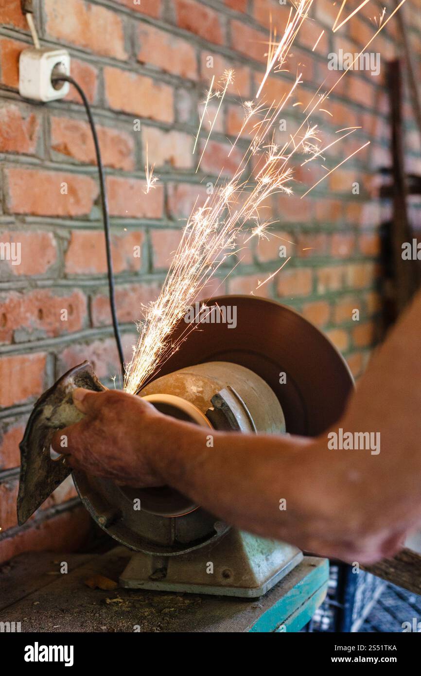peasant sharpens garden tool on electric grindstone in rural shed Stock ...