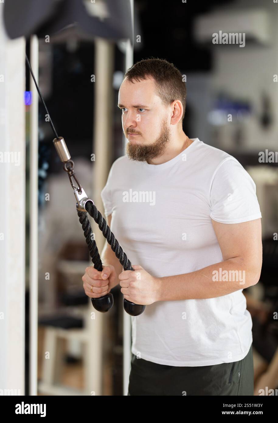 Man in gym performs exercises for arm muscles using cable crossover ...