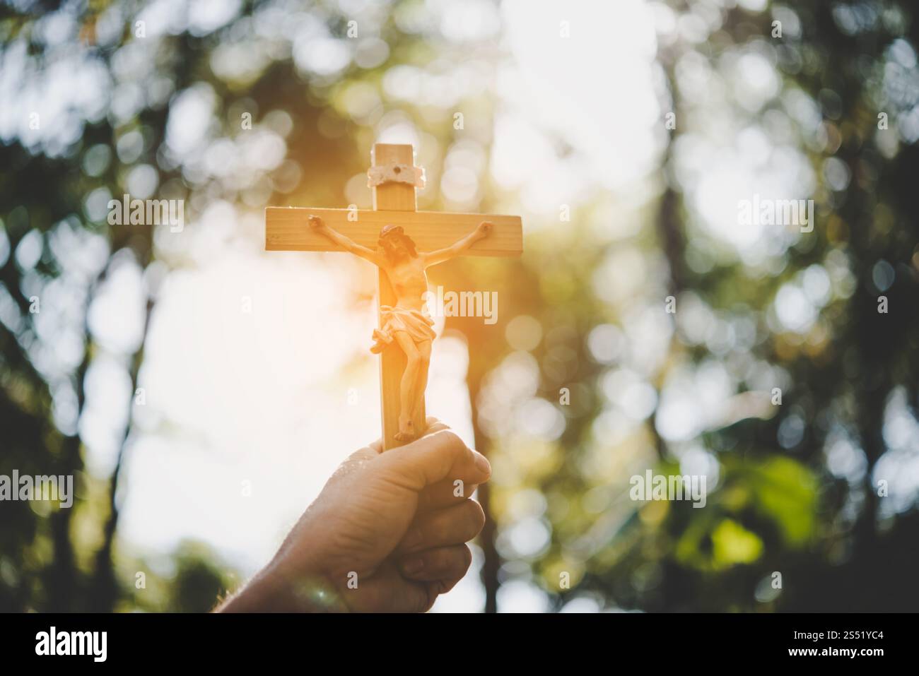 Male hands holding wooden jesus cross over into the sky with nature ...