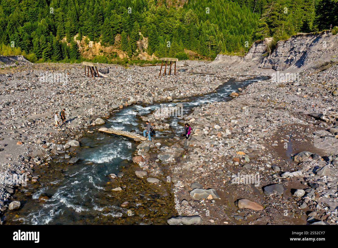 Hikers Crossing a Stream Amidst Rocky Terrain and Lush Green Forests ...