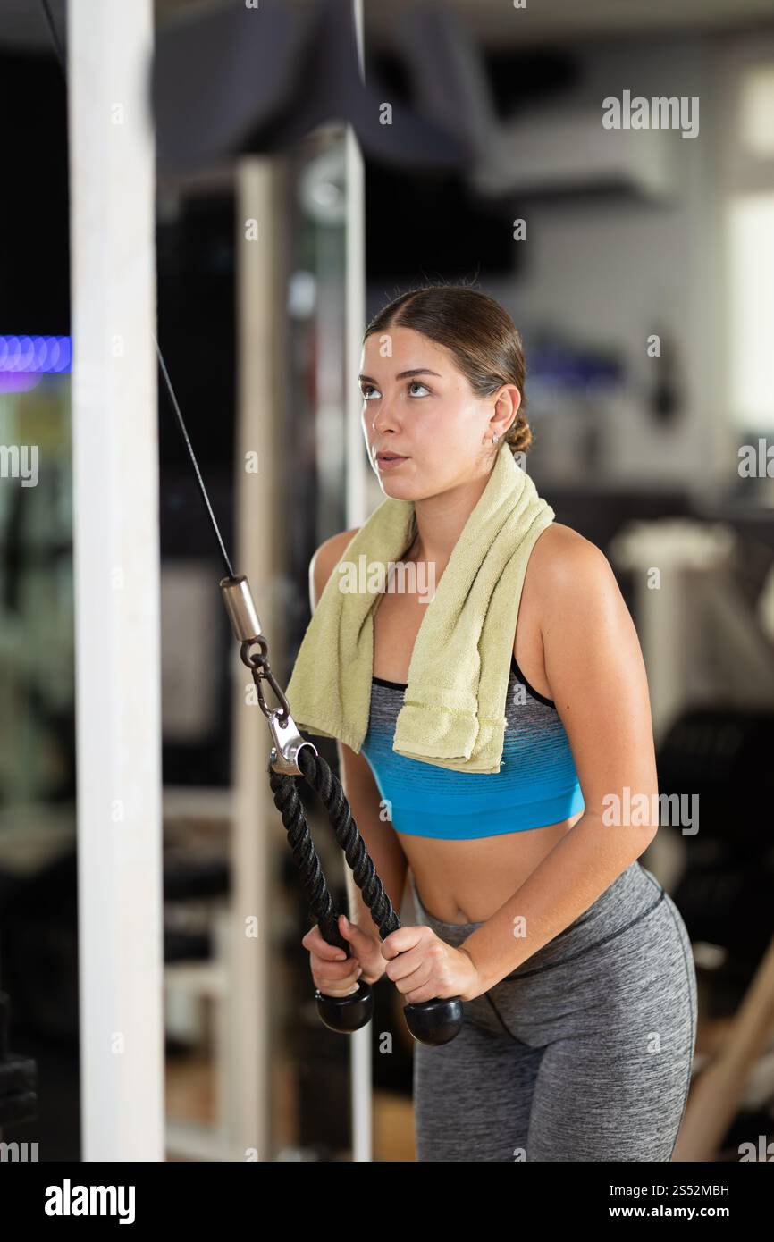 Girl in gym performs exercises for arm muscles using cable crossover ...