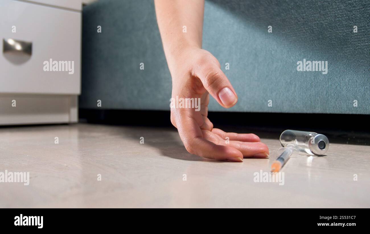 Closeup image of female hand falling on floor next to empty syringe and ...