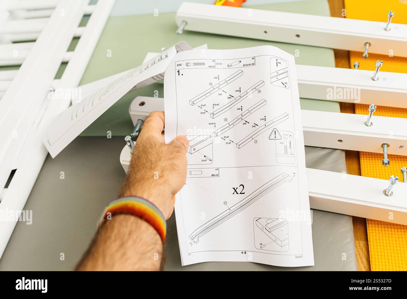 A hand holding an open instruction manual over white furniture pieces ...