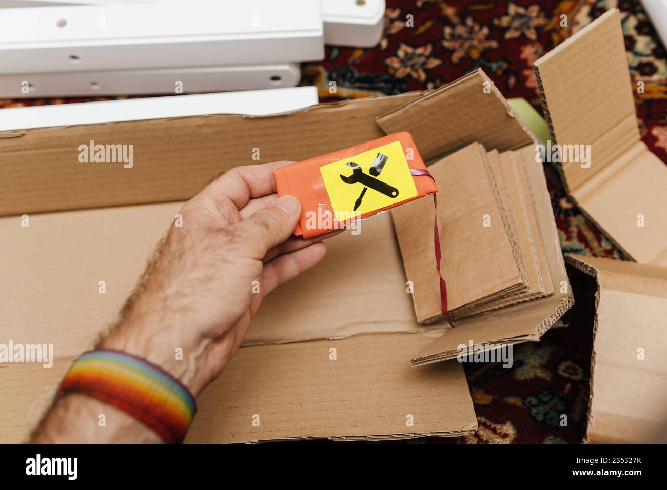Hand holding a toolkit wrapped in orange paper with a warning label ...