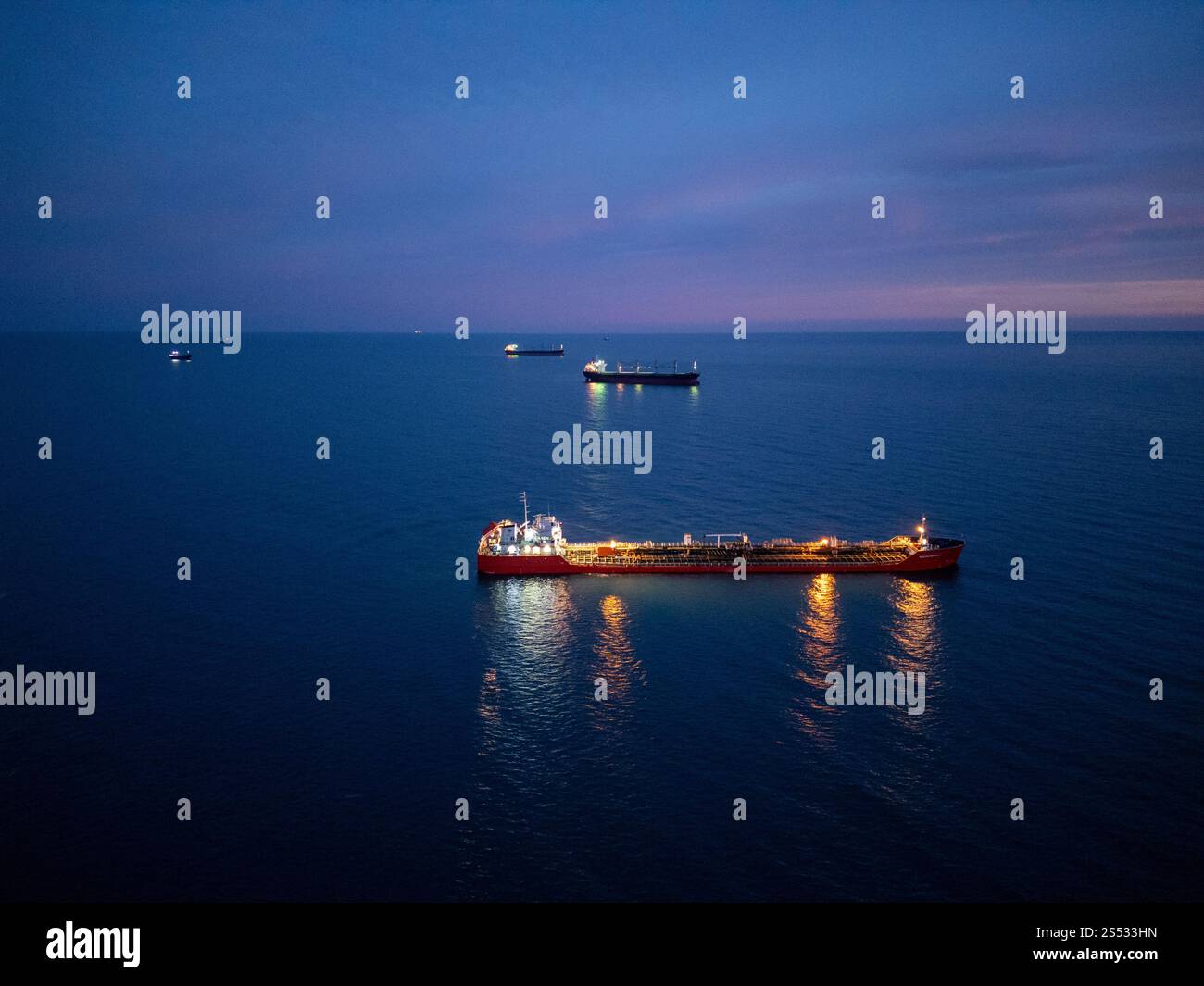 Aerial view of a brightly lit tanker ship on the sea during dusk ...